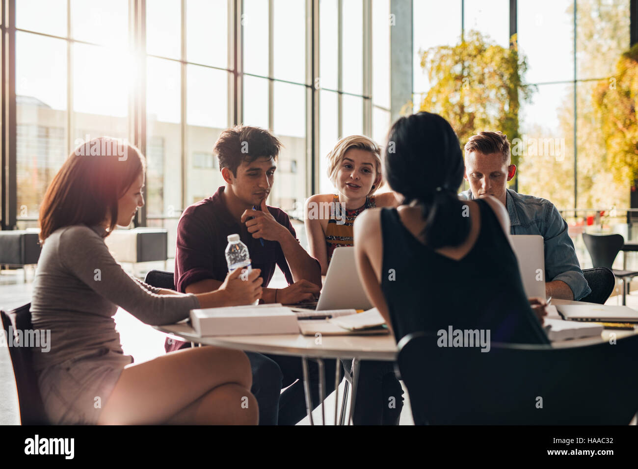 Young students sitting around a table in library with books and laptop ...