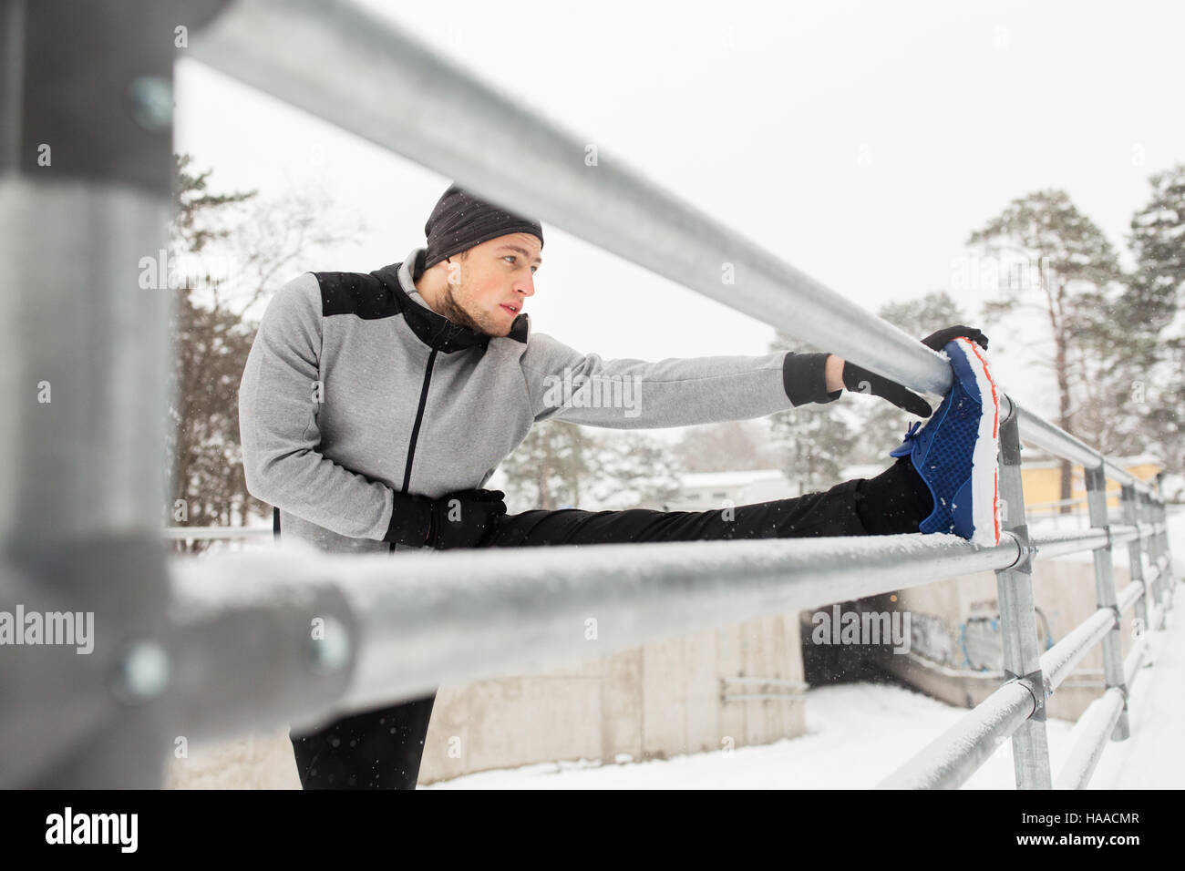 sports man stretching leg at fence in winter Stock Photo - Alamy