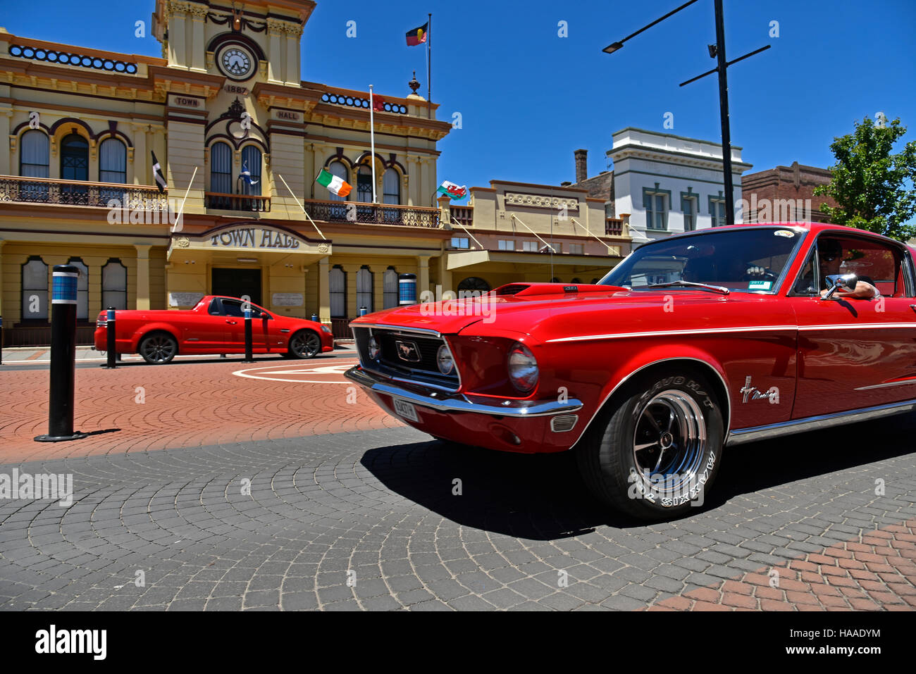 classic red mustang car passes in front of the historic Glen Innes town ...