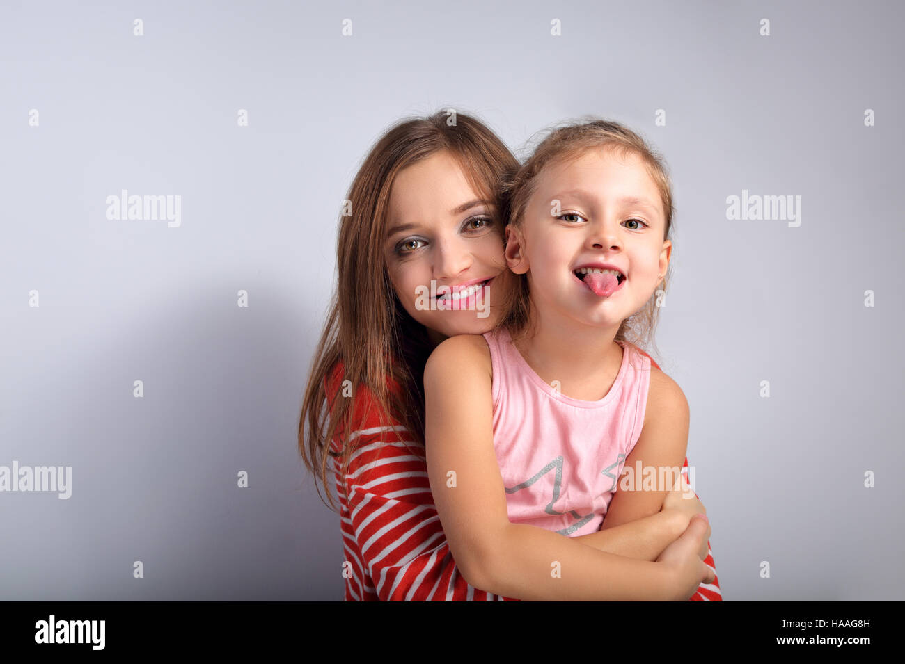 Happy smiling mother hugging with love her frolic grimacing kid showing ...