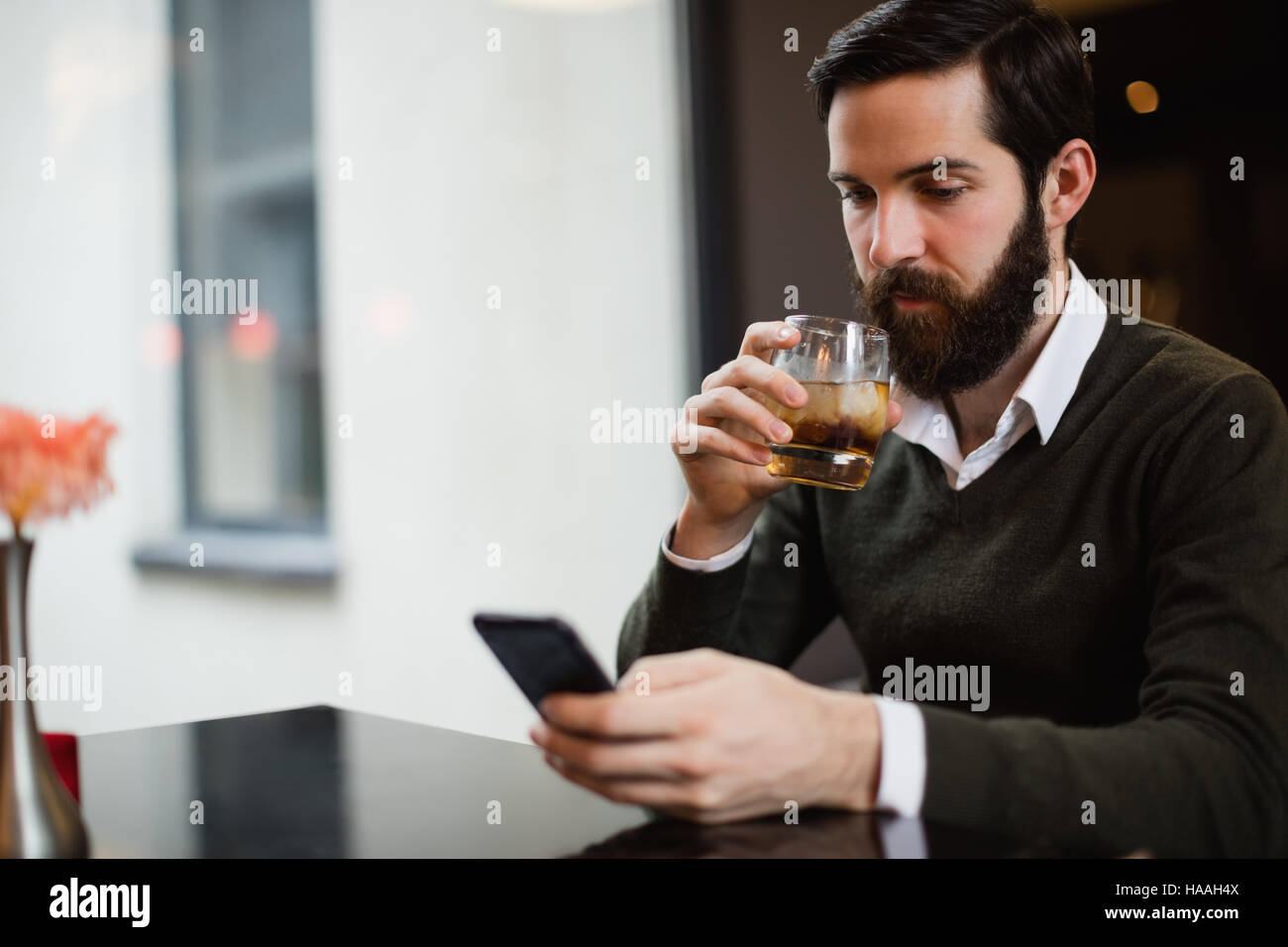 Man having glass of drink while using mobile phone Stock Photo - Alamy