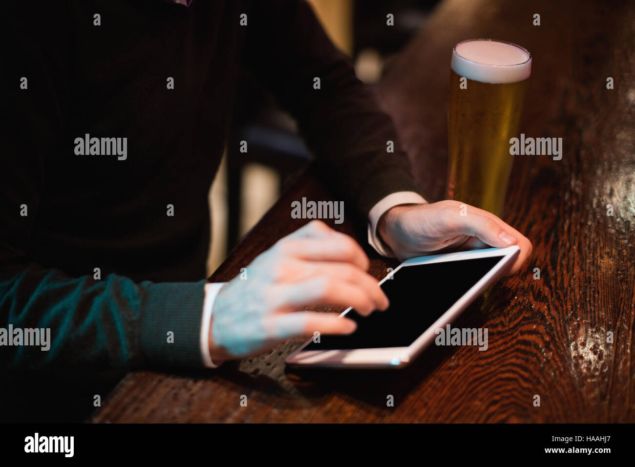 Man using digital tablet with glass of beer on counter Stock Photo - Alamy