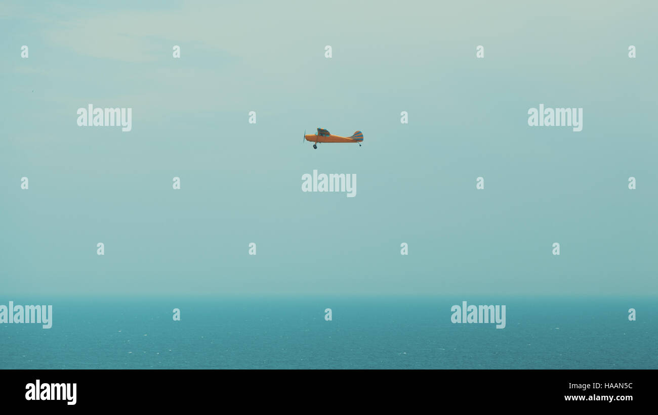 Orange one engine prop plane with teal stripes flying over the misty ...