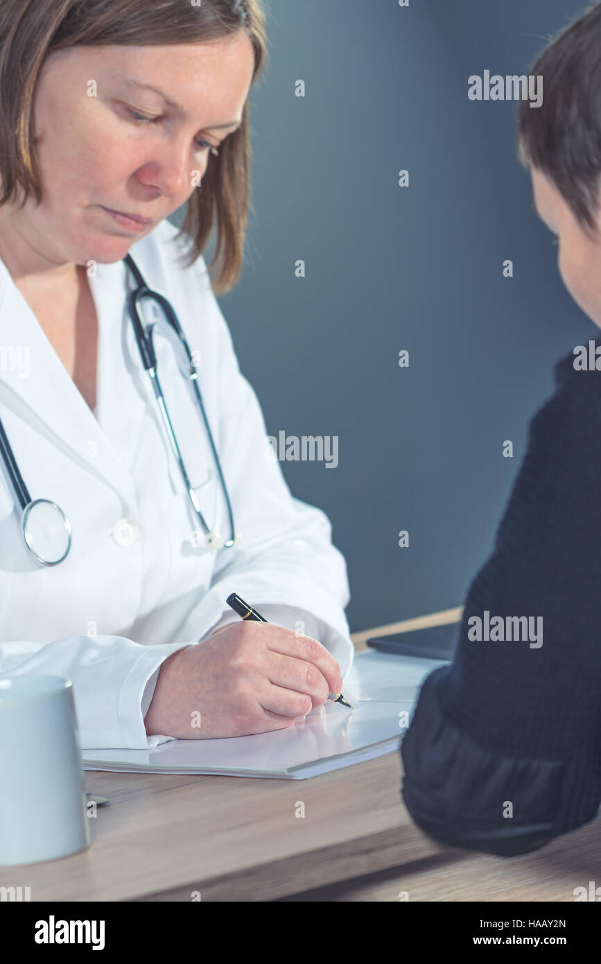 Doctor writing medicine therapy prescription to female patient in ...