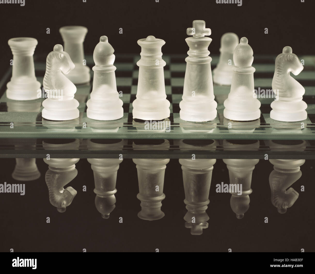 Old glass chess pieces on board reflected on black mildly textured ...