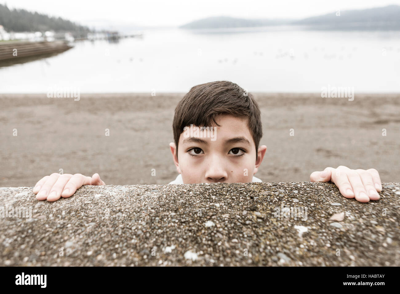 A conceptual image of a young boy peering over a wall by a lake Stock ...