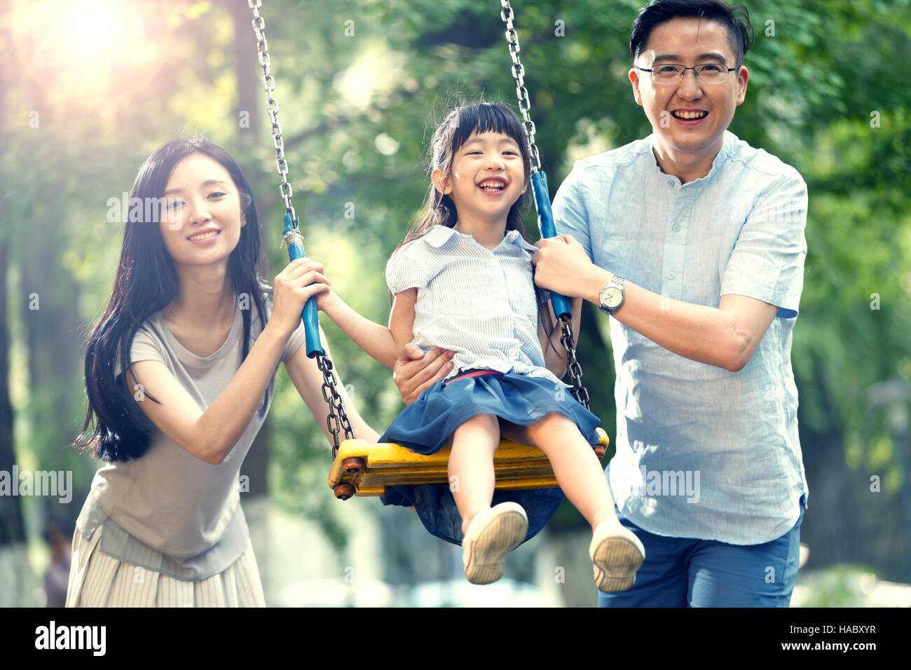 Happy family of three swing Stock Photo - Alamy