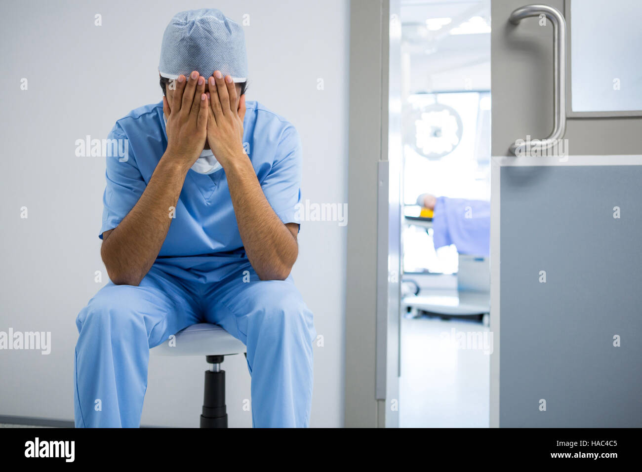 Tensed surgeon sitting with hands on face in corridor Stock Photo - Alamy