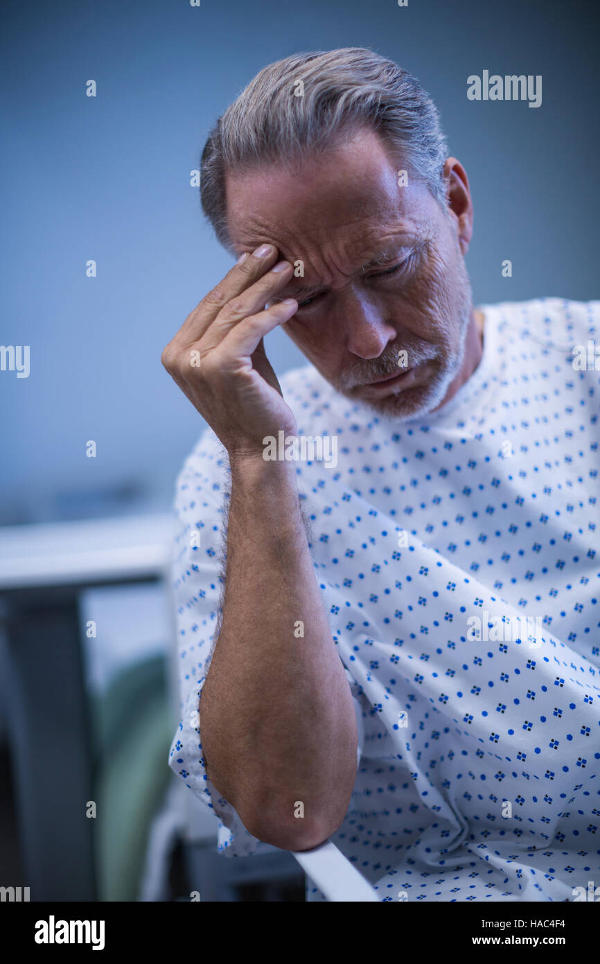 Sad patient sitting on chair with hand on head Stock Photo - Alamy