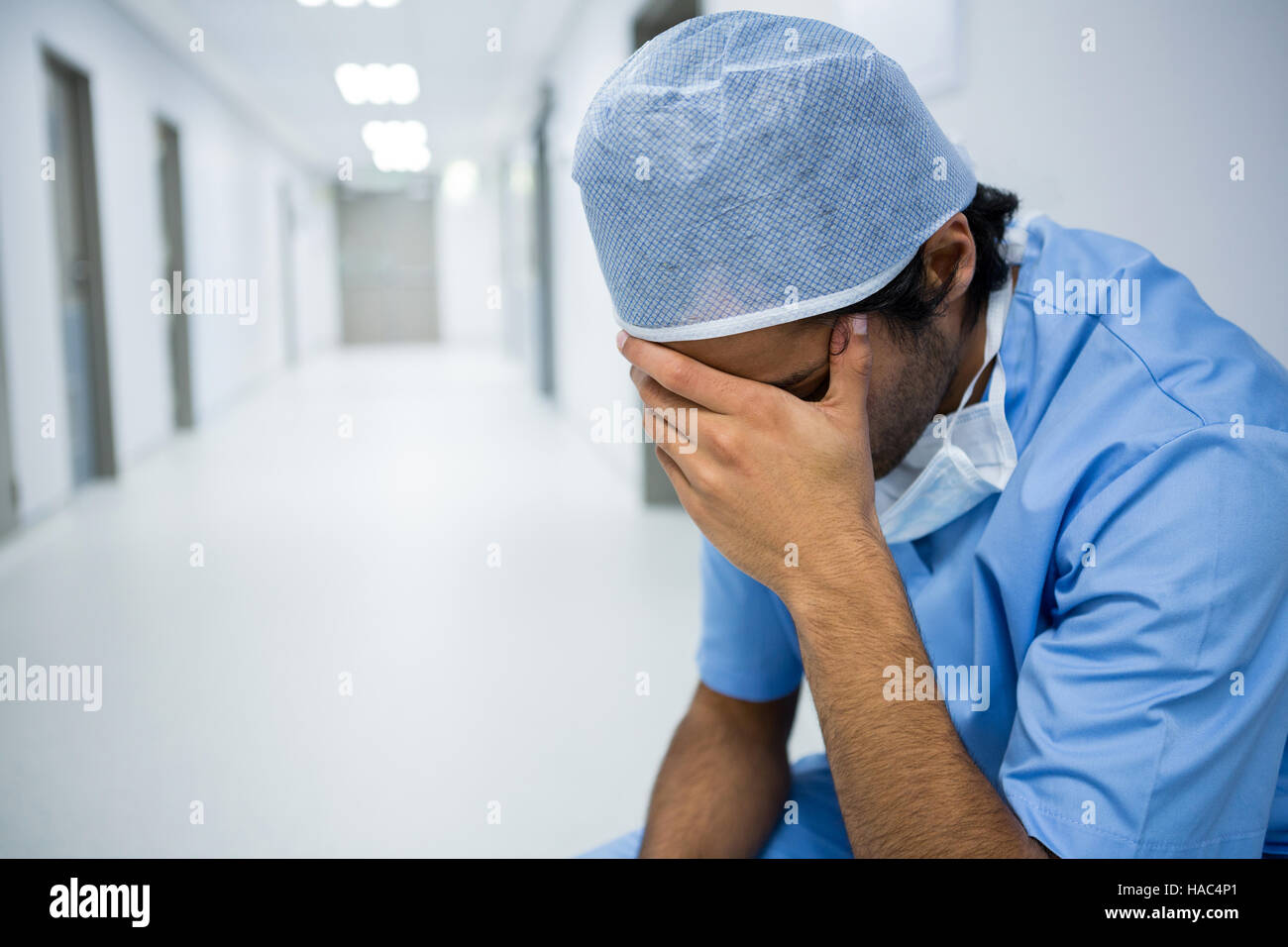 Tensed surgeon sitting with hand on forehead in corridor Stock Photo ...