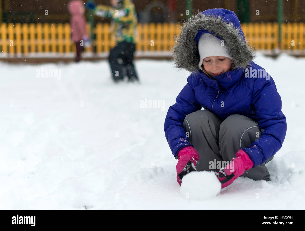 Little girl rolling snowball in winter Stock Photo - Alamy