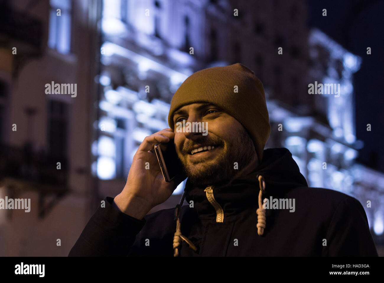 Smiling man talking on the phone at night. Evening city lights on the ...