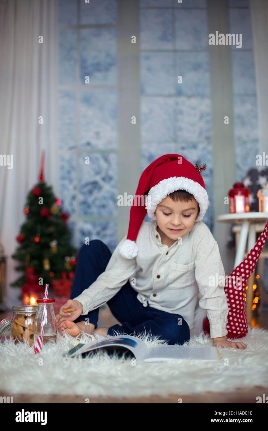 Cute preschool child, boy, reading a book and eating cookies at home ...