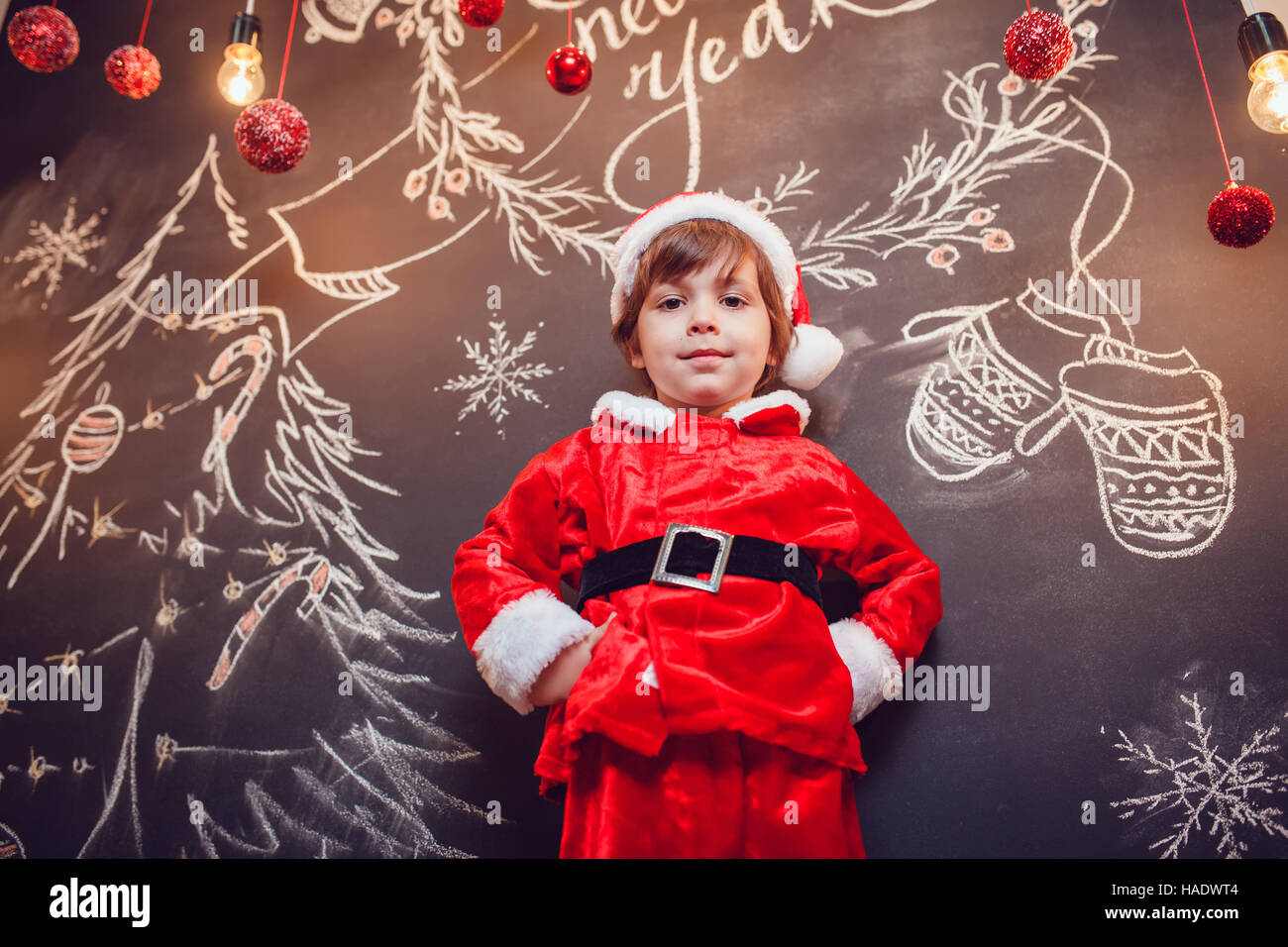 Little boy dressed as Santa Claus standing on dark background with ...