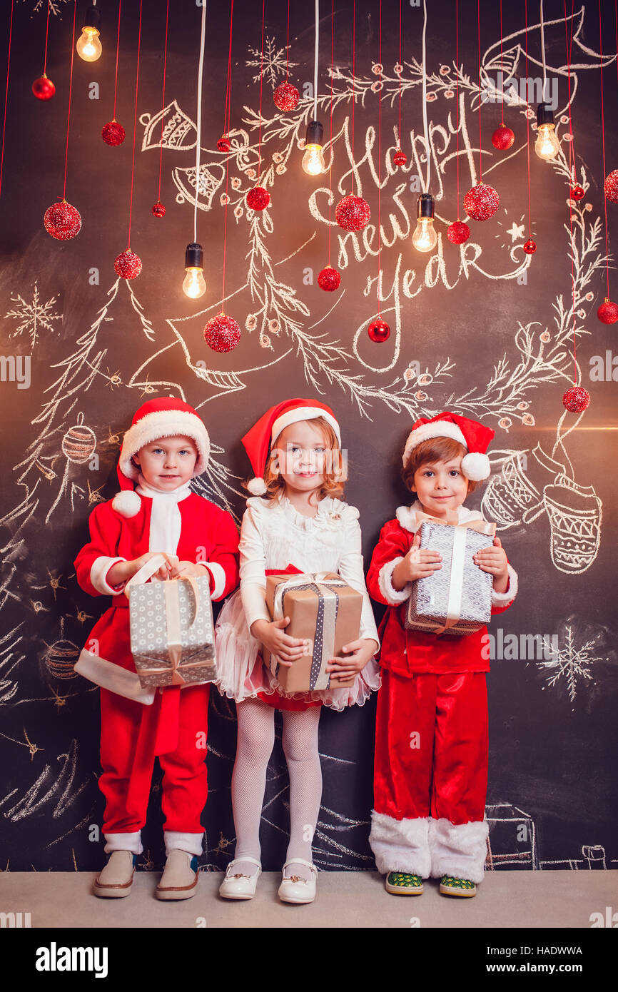Children dressed as Santa Claus standing and holding gifts on dark ...