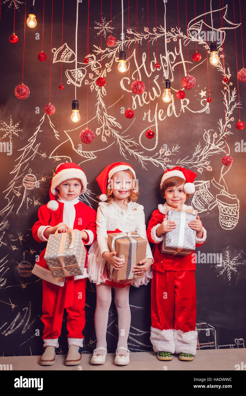 Children dressed as Santa Claus standing and holding gifts on dark ...