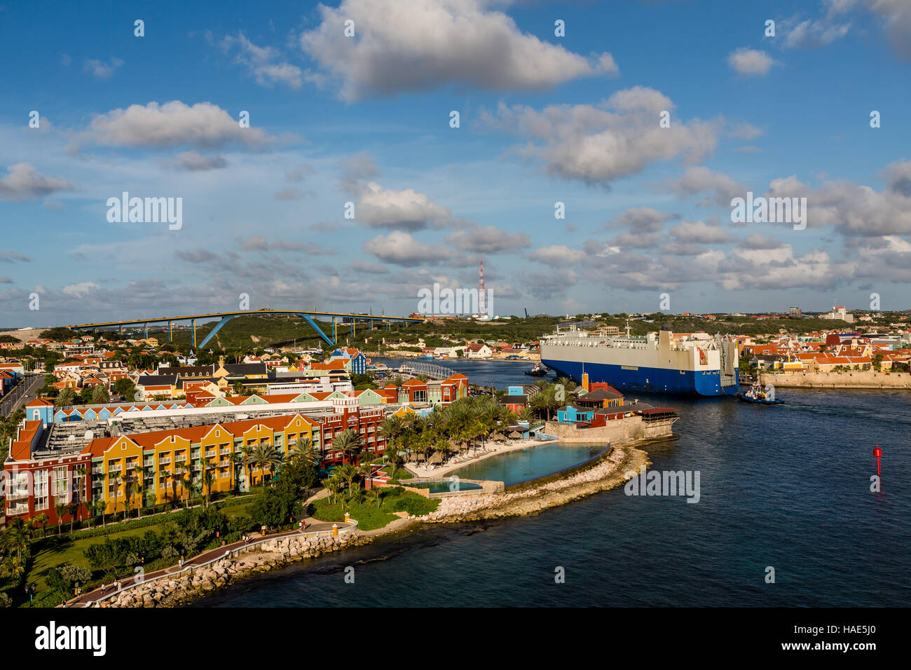 A huge container ship being led into the narrow harbor on Curacao past ...