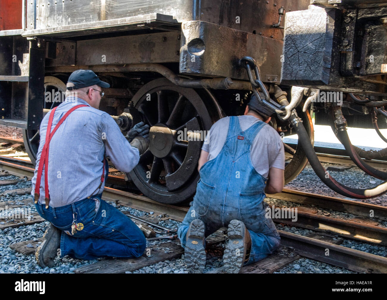 Two train workers repairing old classic train in blue overalls on ...