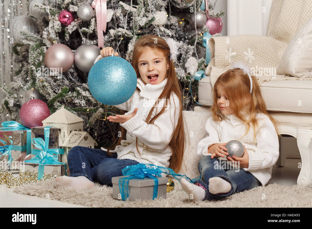 Two sisters playing with Christmas decorations and presents sitting on ...