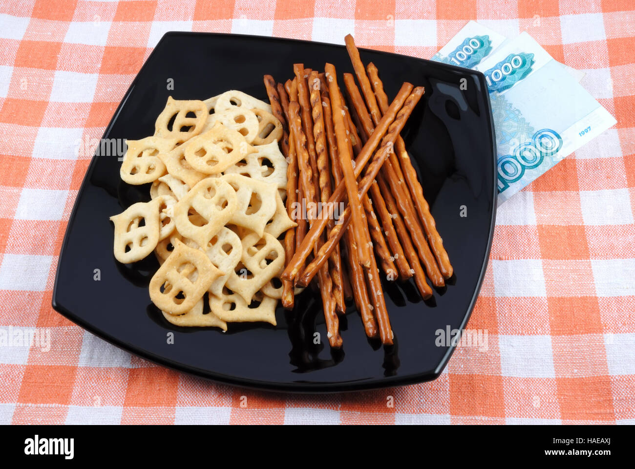 Mini crackers and salty grain sticks to beer on a black plate and money ...