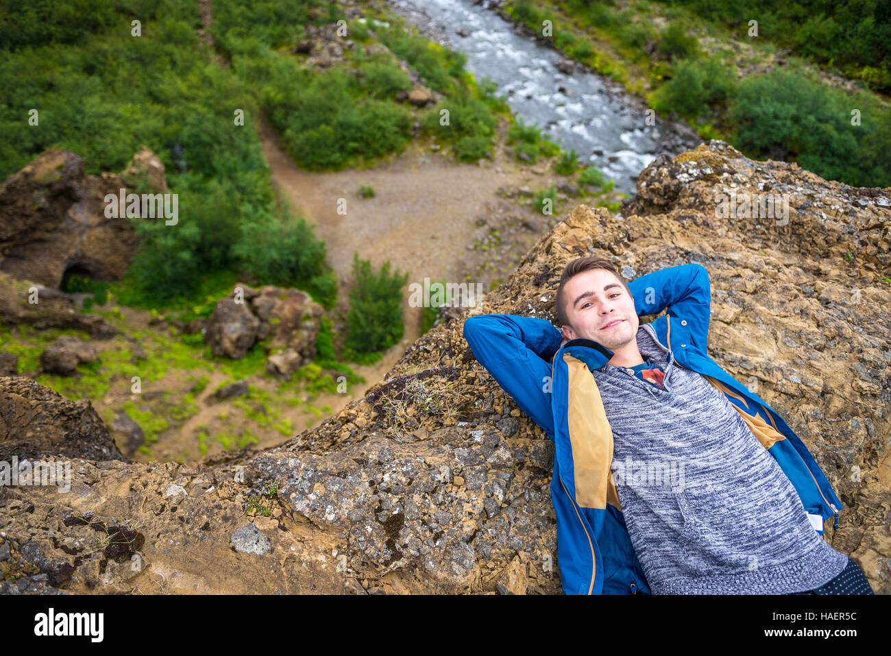 Happy young man lying on the edge of the cliff near Glymur waterfall in ...