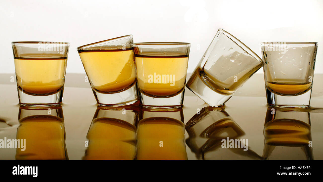 Shot glasses of whiskey are reflected in a shiny bar surface as they ...