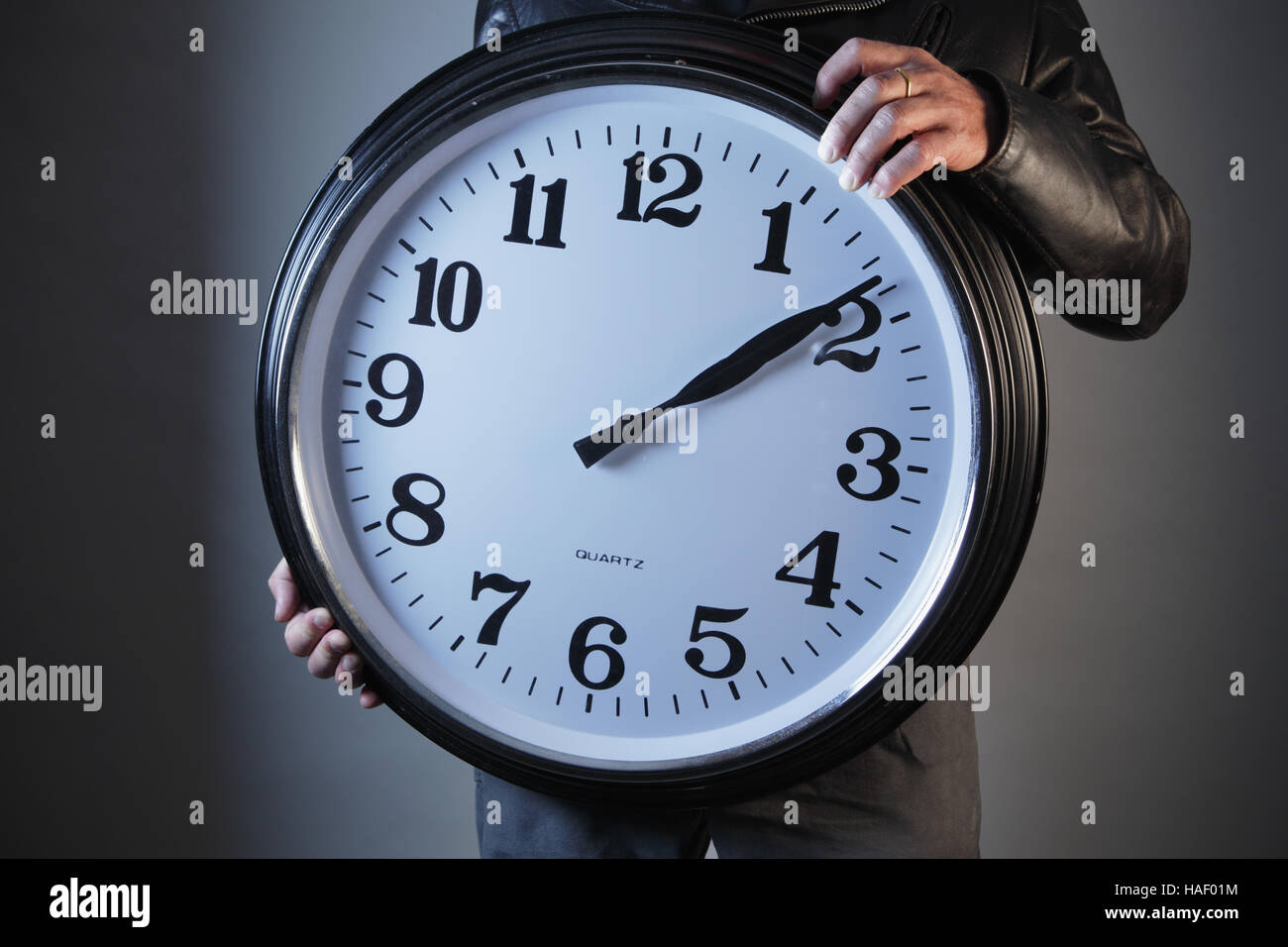 Male in leather jacket holding giant clock Stock Photo - Alamy