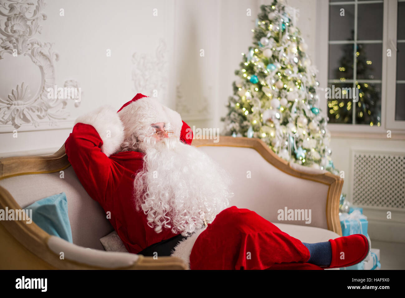 Santa Claus relaxing on sofa against christmas tree at home Stock Photo ...
