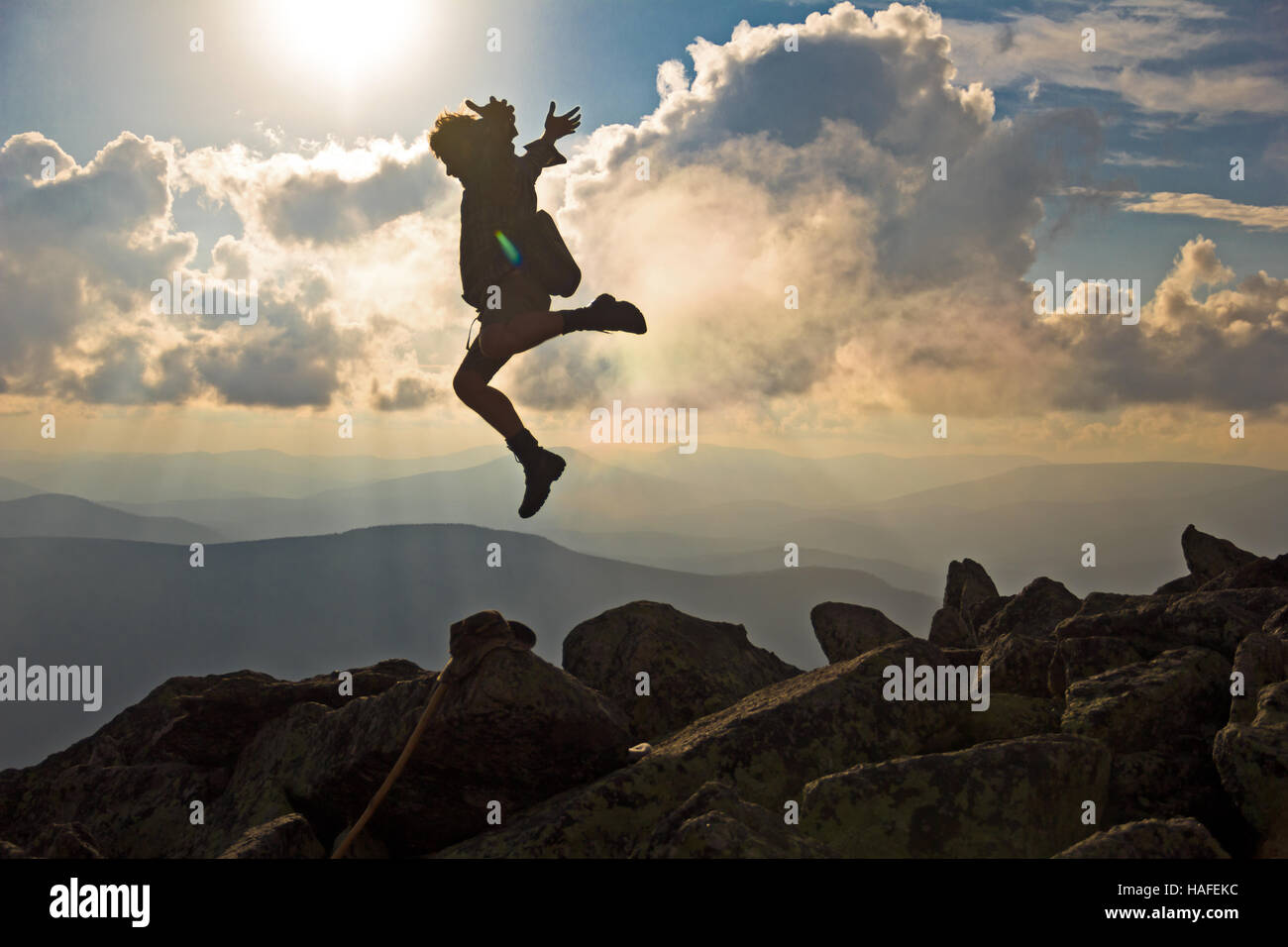 Hiker with backpack jumping over rocks sunset sky on the background ...