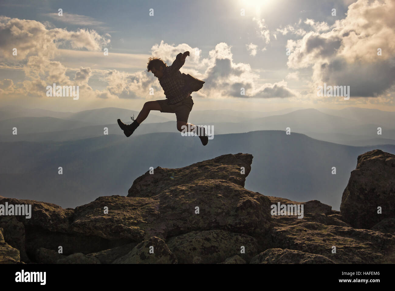 Hiker with backpack jumping over rocks sunset sky on the background ...