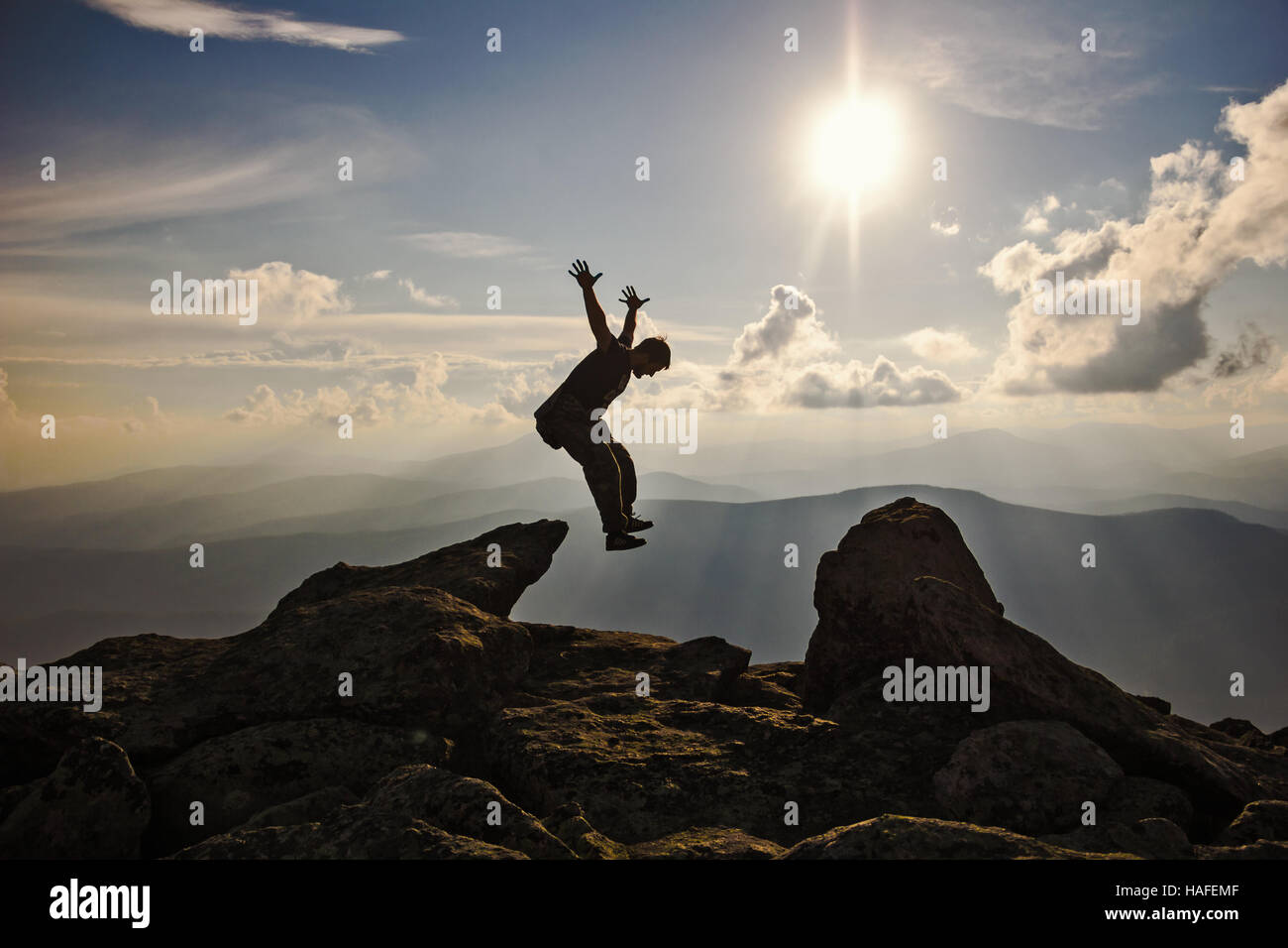 Hiker with backpack jumping over rocks sunset sky on the background ...