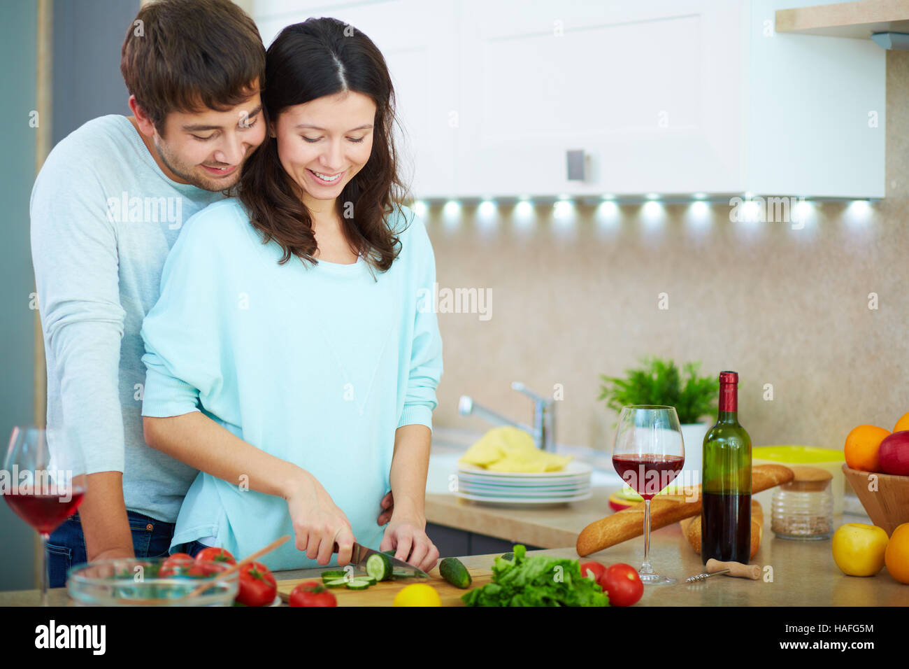 Young woman cooking breakfast while her husband standing by her side ...