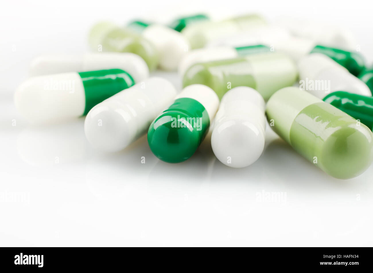 Medical theme. Bright white and green capsules on the white surface ...