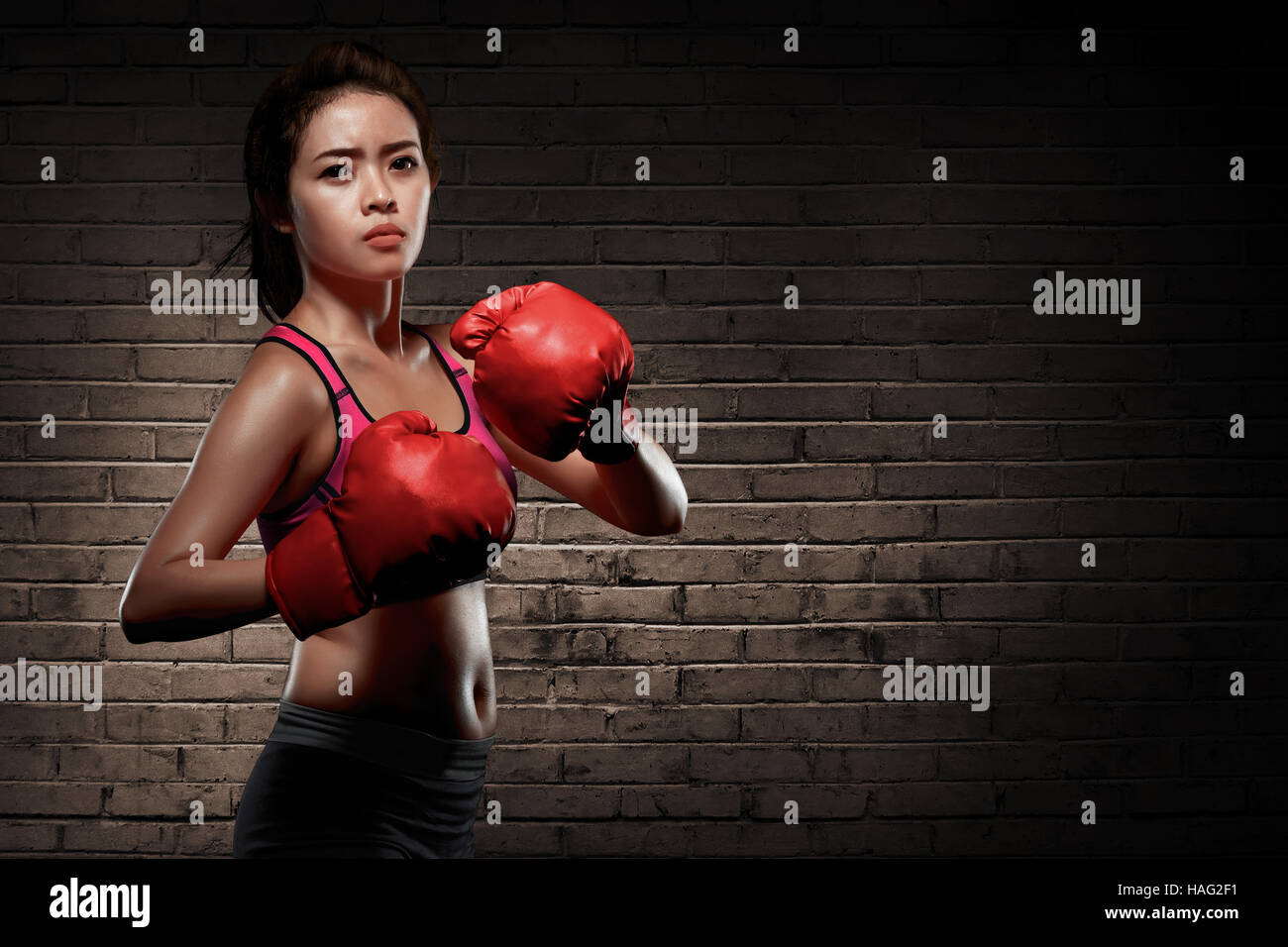 Attractive asian female boxer at training against brick wall background ...