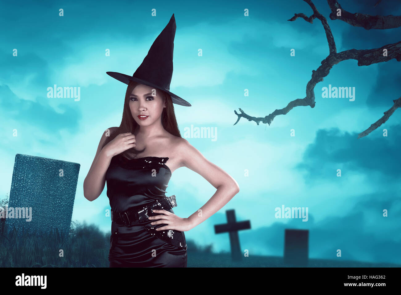 Young asian witch woman with hat standing around in a cemetery at night ...