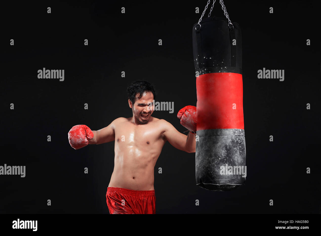 Muscular asian man boxer training with punching bag over black ...