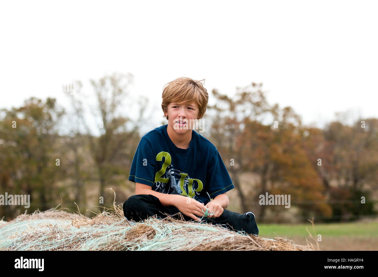 Long haired boy sitting on hay out in the country looking sideways ...