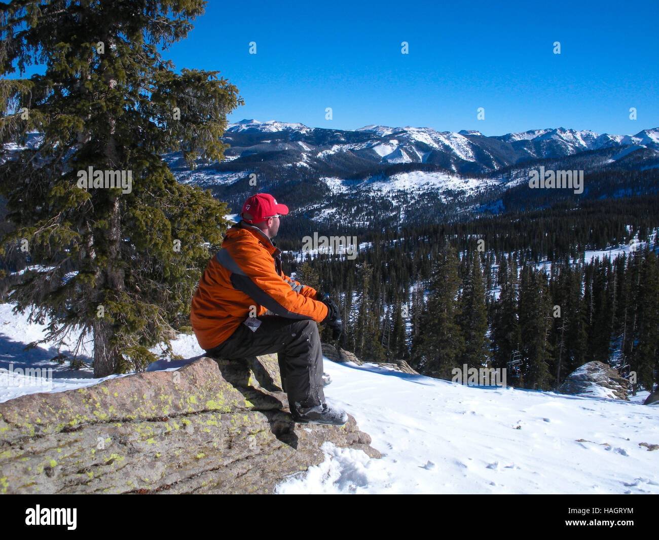 Man sitting on rock in the snow peering at the mountains Stock Photo ...