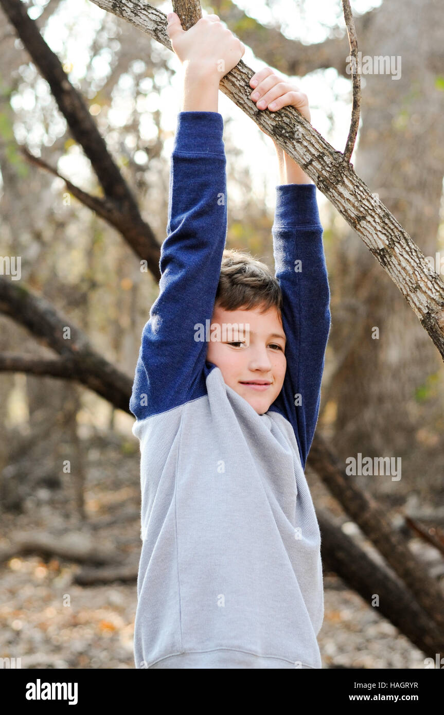 Outdoor portrait of young handsome boy hanging from a branch of a tree ...
