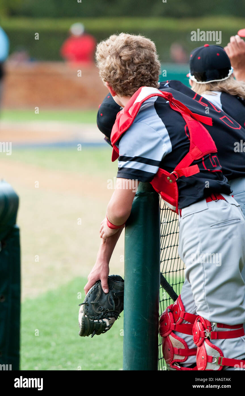 Youth baseball team and catcher standing in the dugout watching the ...