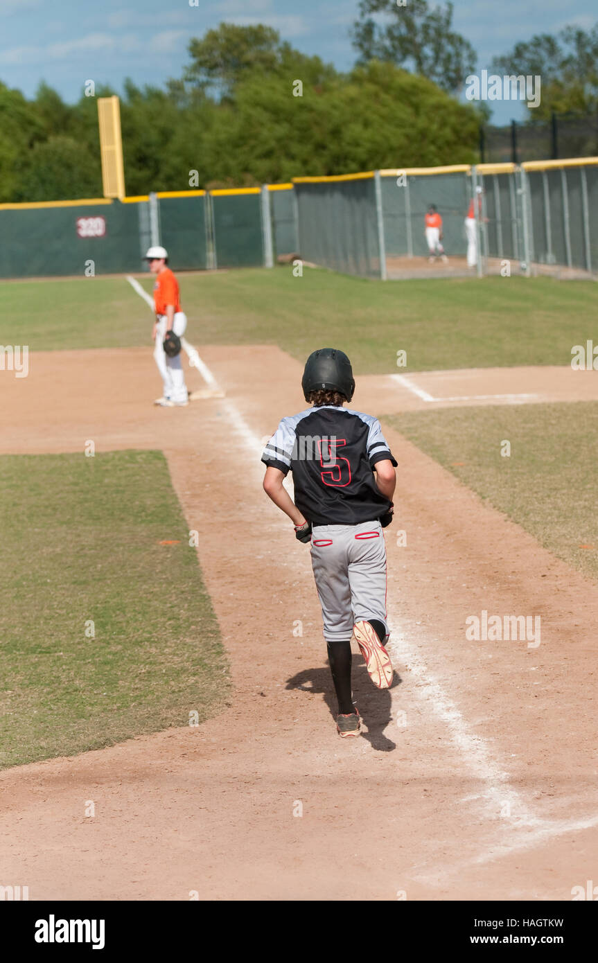 Youth baseball kid running to first base after a walk at home plate ...