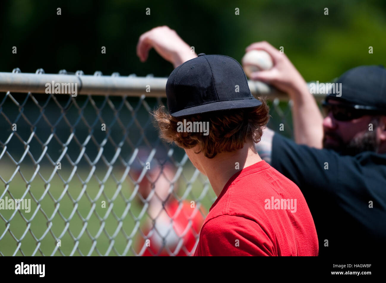 Teen boy and middle-aged father leaning on fence watching baseball game ...