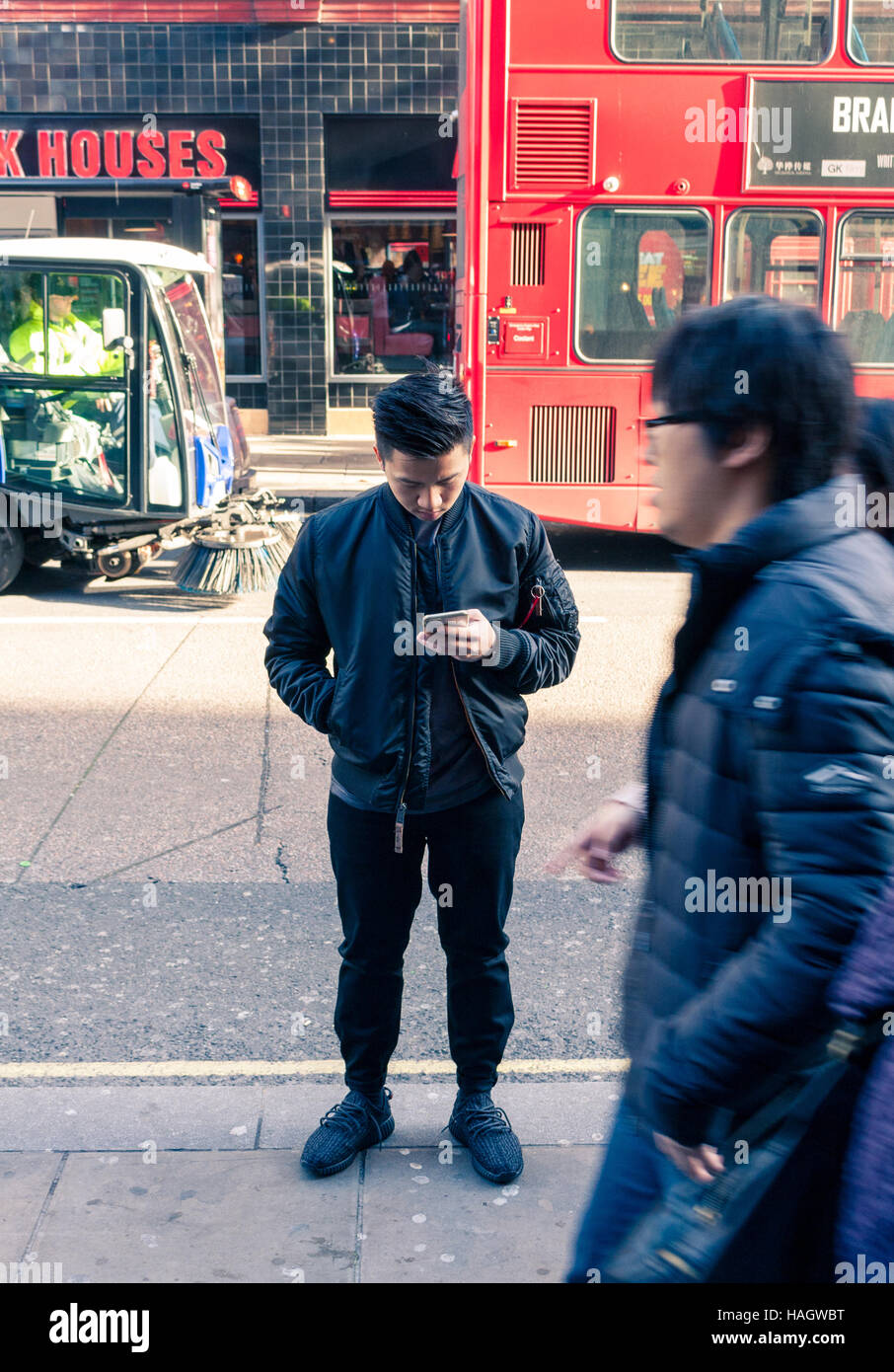 A young man dressed in black, stood on the pavement whilst using a ...