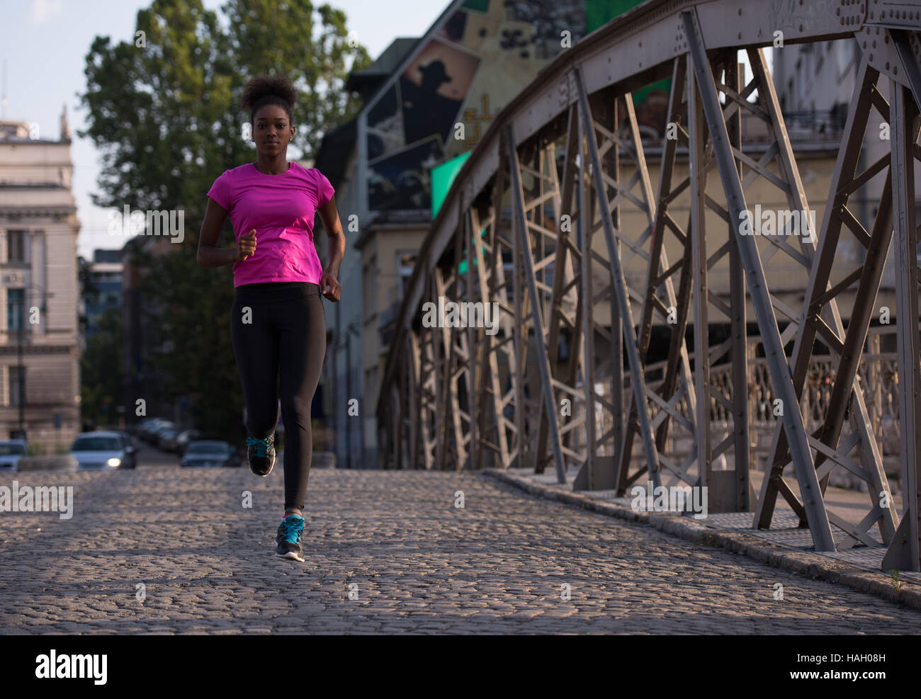 Young sporty african american woman running on sidewalk across the ...
