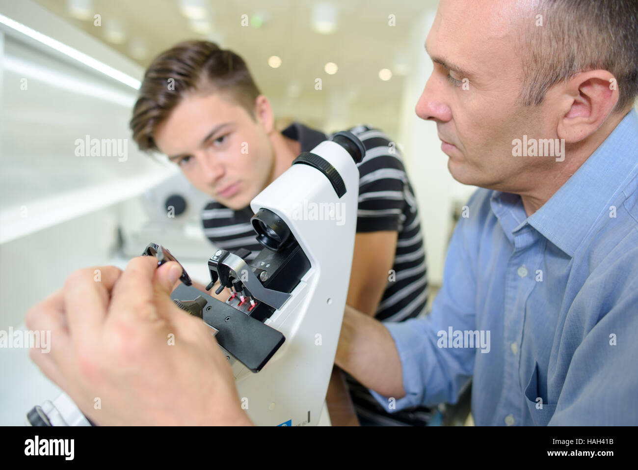 Man setting up microscope, apprentice watching Stock Photo - Alamy