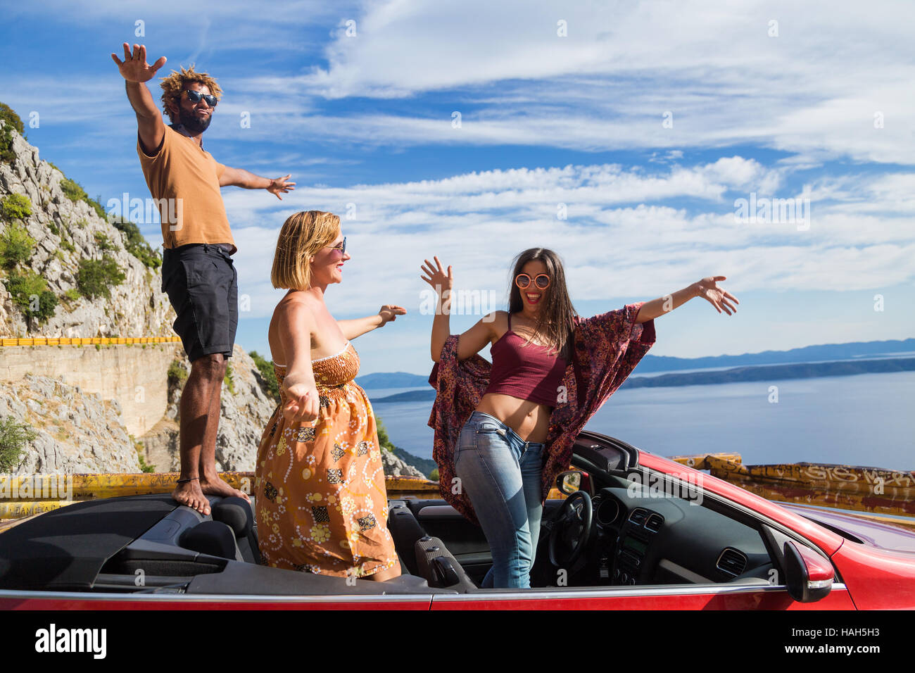 Group of happy young people standing in the red convertible car and ...