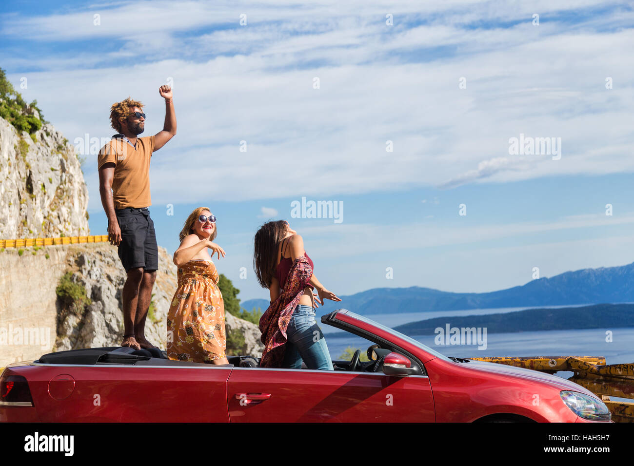 Group of happy young people standing in the red convertible car and ...