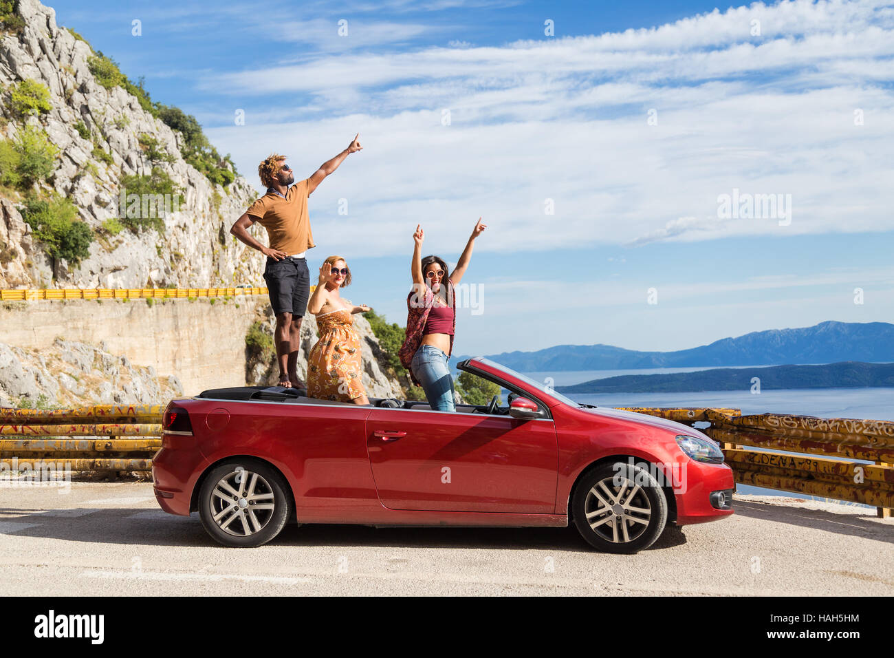 Group of happy young people standing in the red convertible car and ...