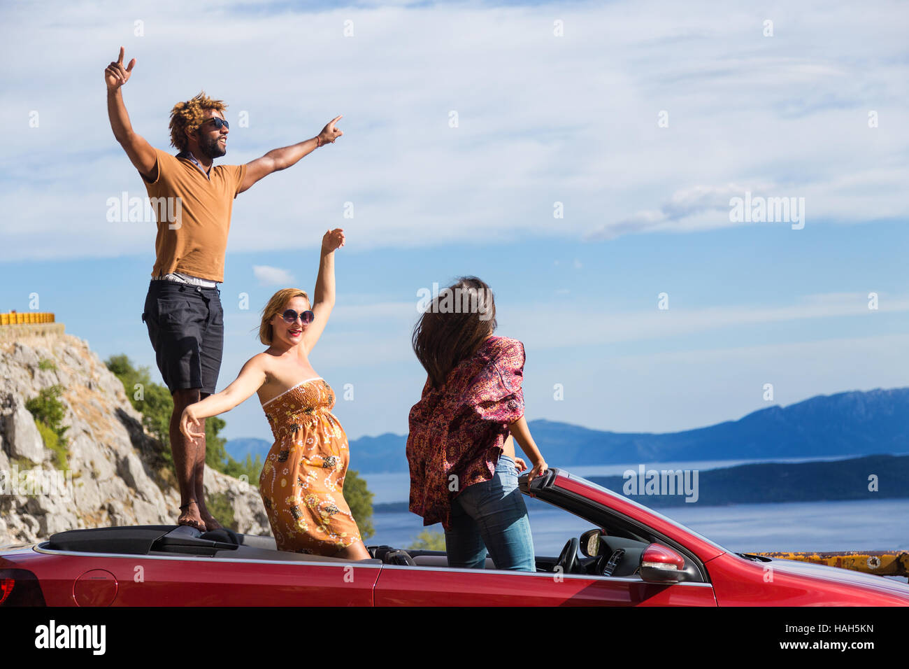 Group of happy young people standing in the red convertible car and ...
