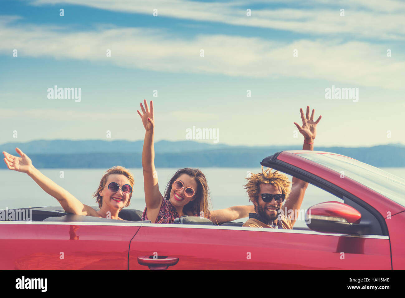 Group of happy young people waving from the red convertible. Vintage ...